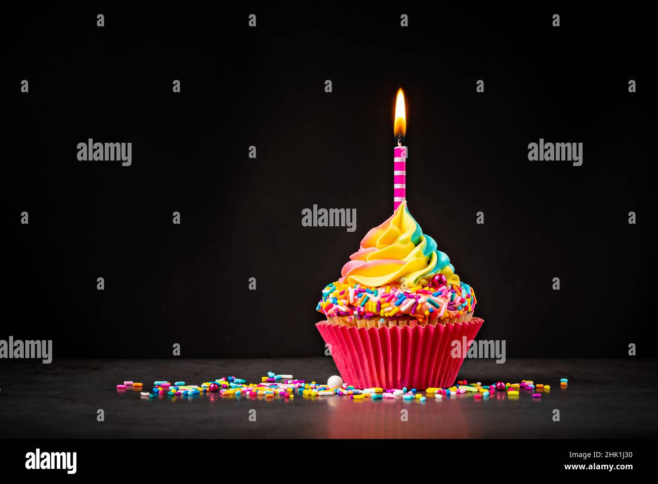 Rainbow Birthday cupcake with a pink candle and colorful sprinkles over ...