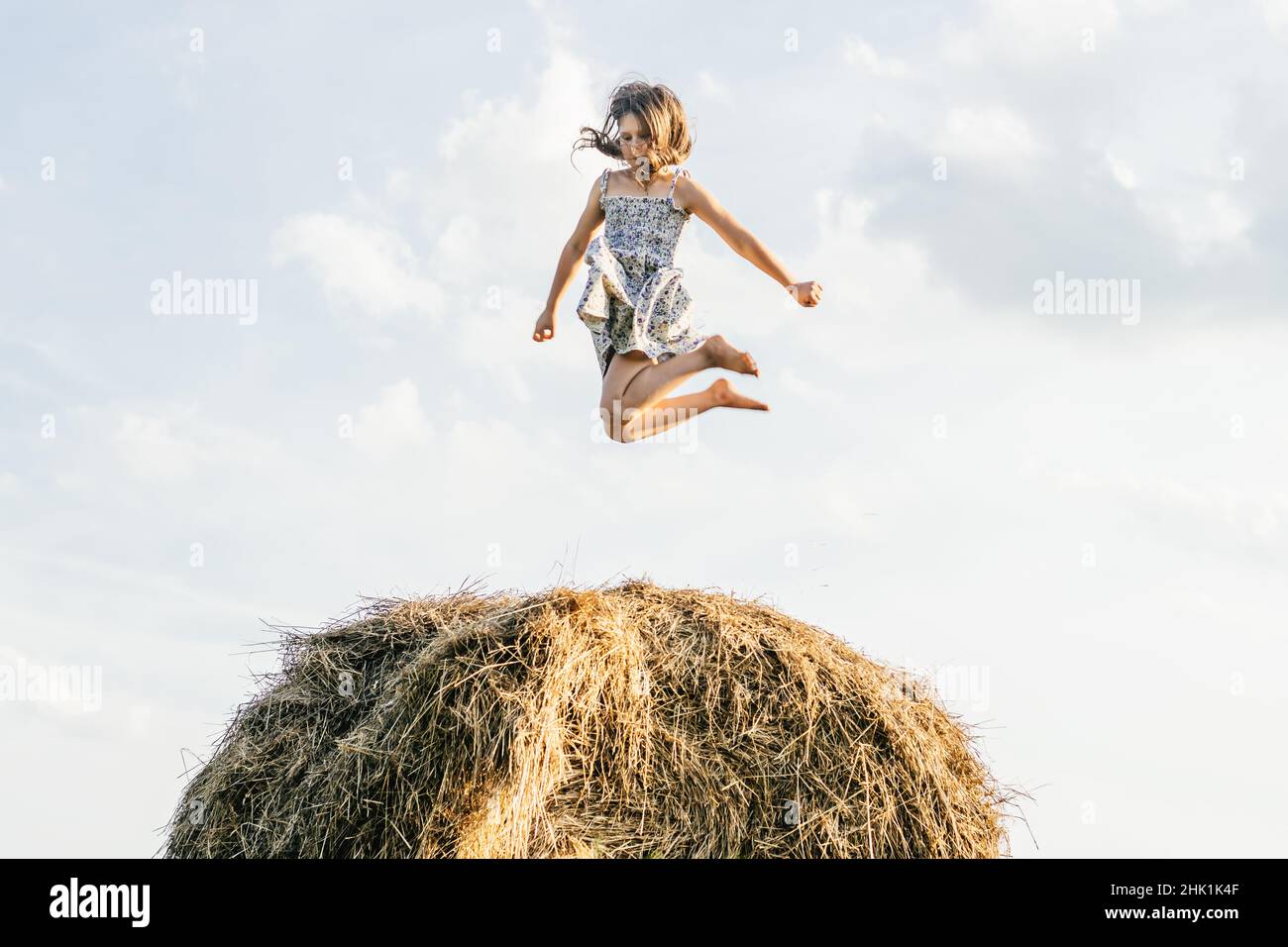Portrait of little girl in dress playing and jumping on haystack in ...