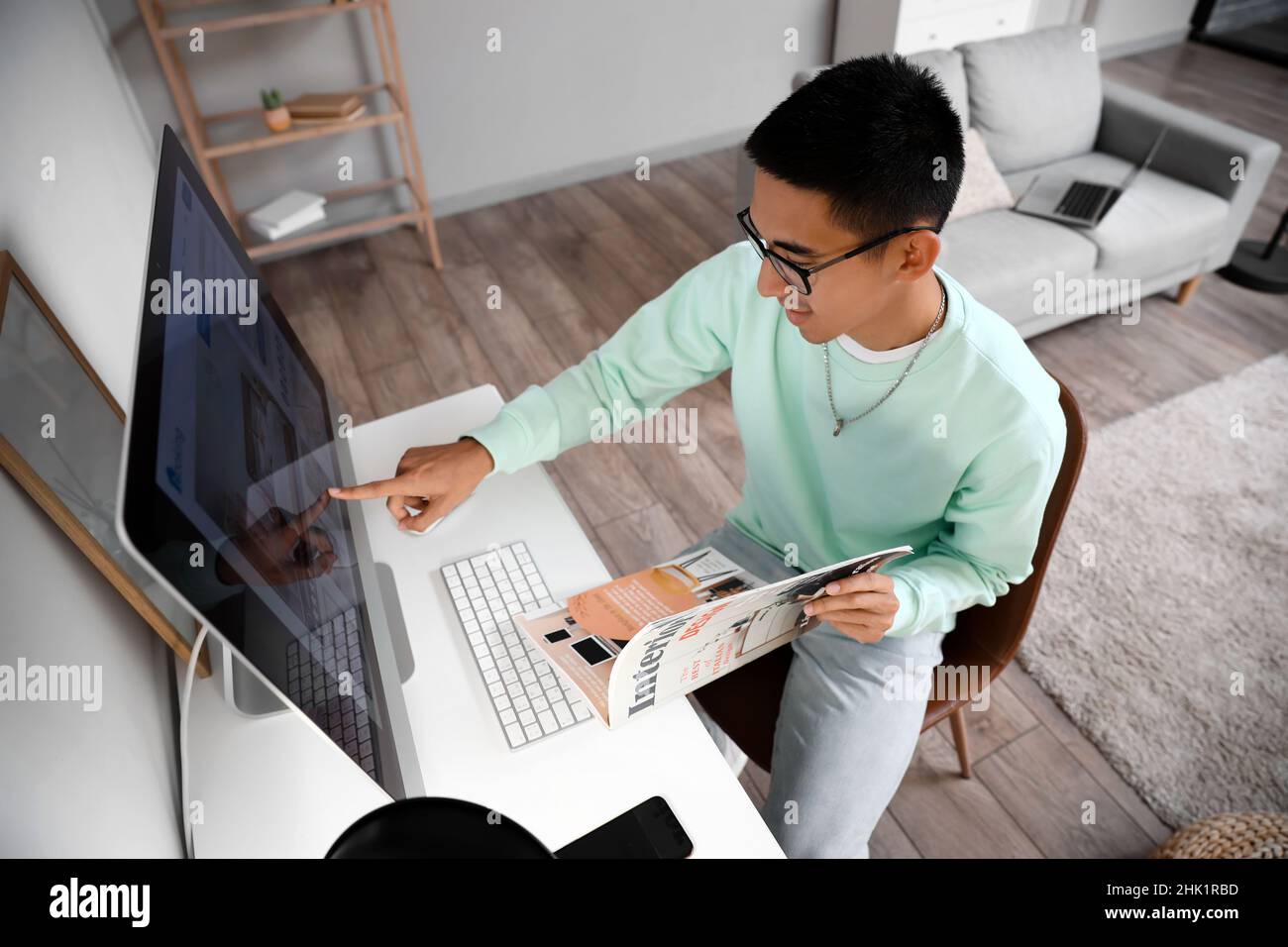 Young man with magazine pointing at computer screen at home Stock Photo ...