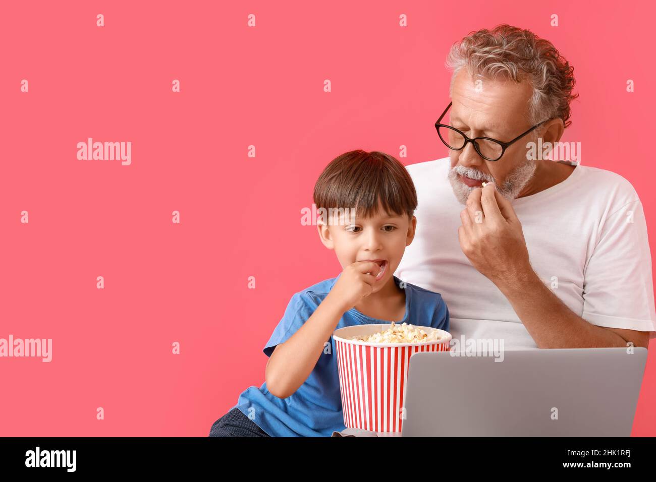 Little boy and his grandfather eating popcorn while watching video on ...