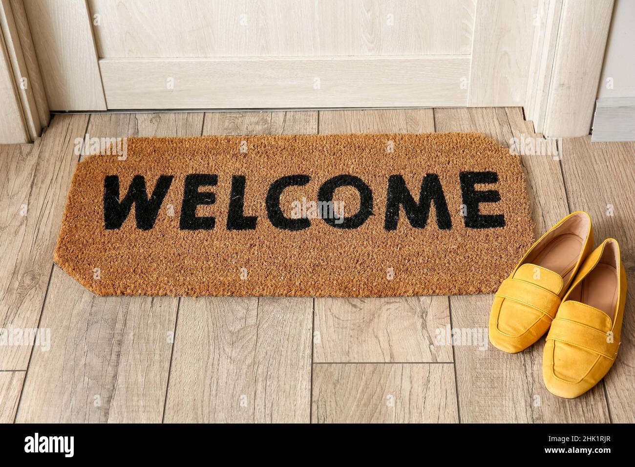 Mat with word WELCOME and female shoes near wooden door in hallway ...