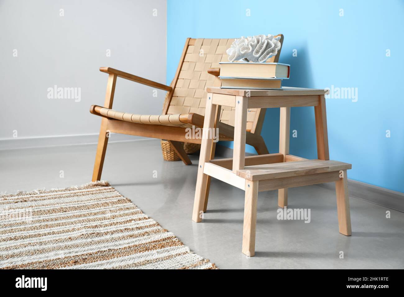 Wooden step stool with decor, books and armchair near blue wall Stock ...