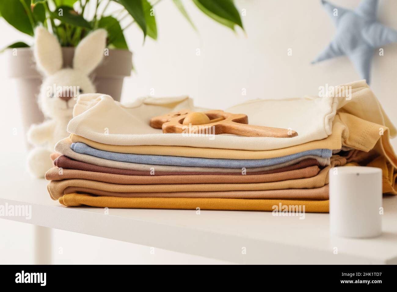 Stack of baby clothes and rattle on self, closeup Stock Photo - Alamy