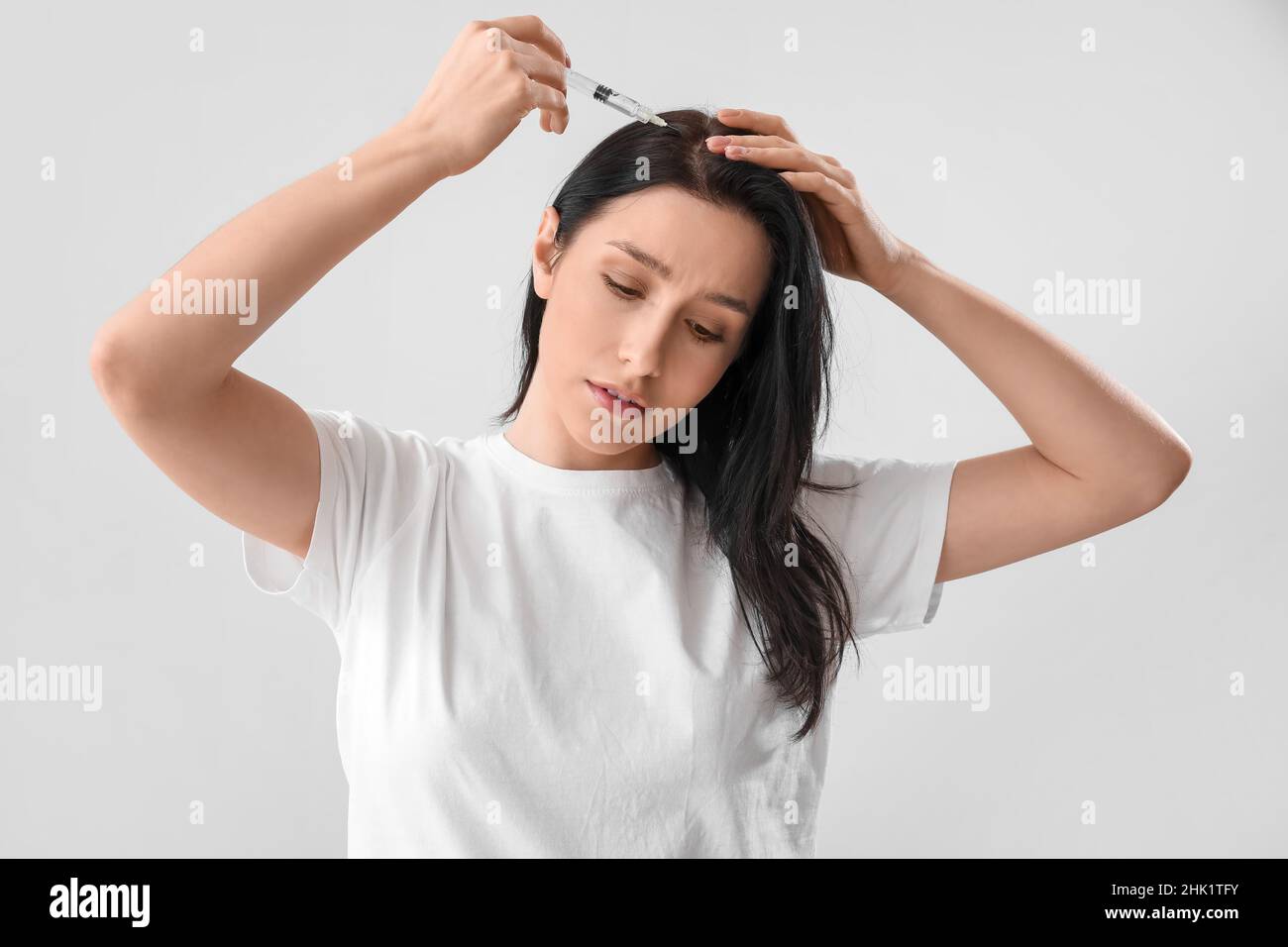 Young woman with hair loss problem giving herself injection on light ...