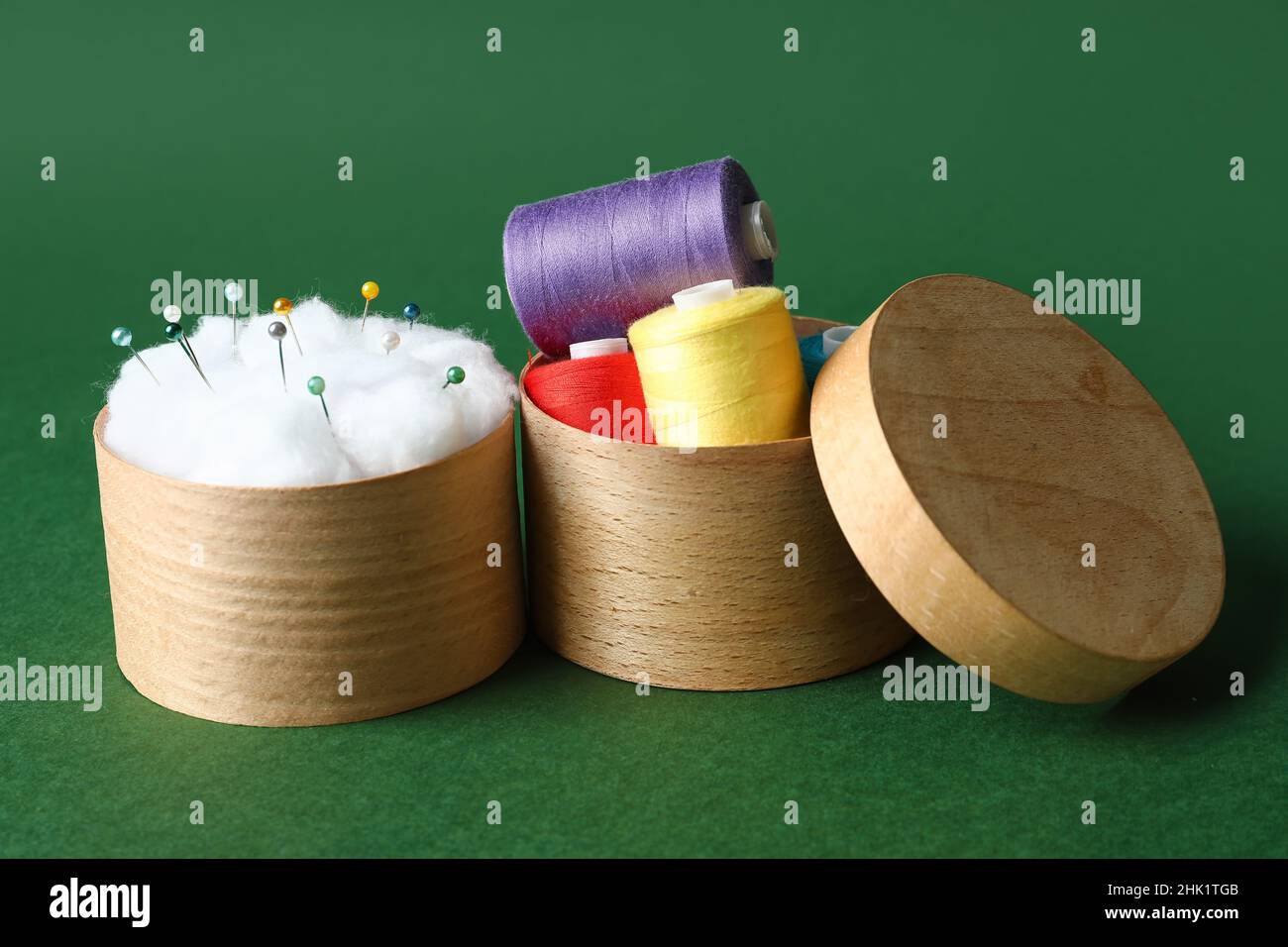 Wooden boxes with sewing thread spools and pins on color background ...