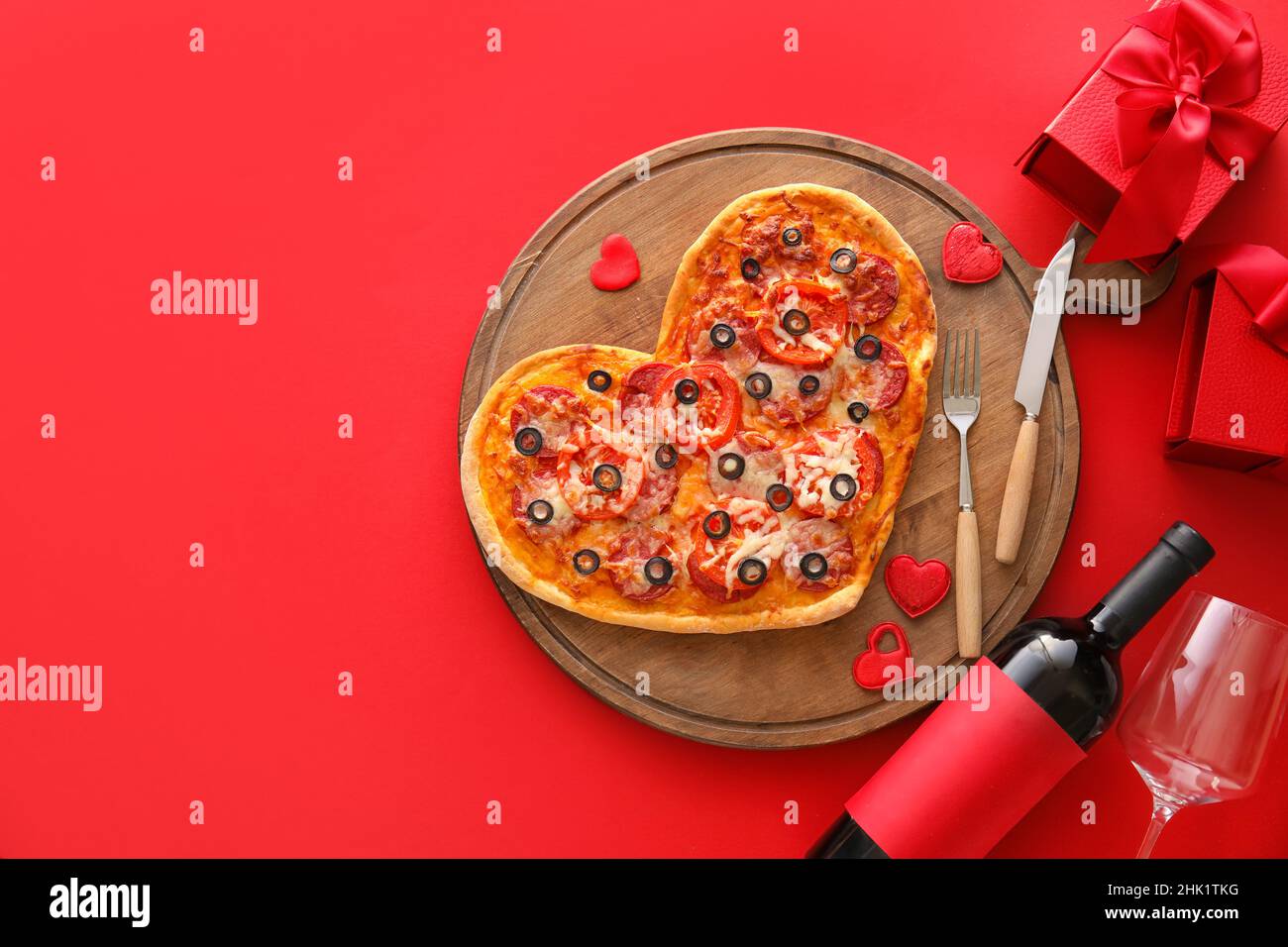 Wooden board with tasty heart-shaped pizza, bottle of wine and gift ...