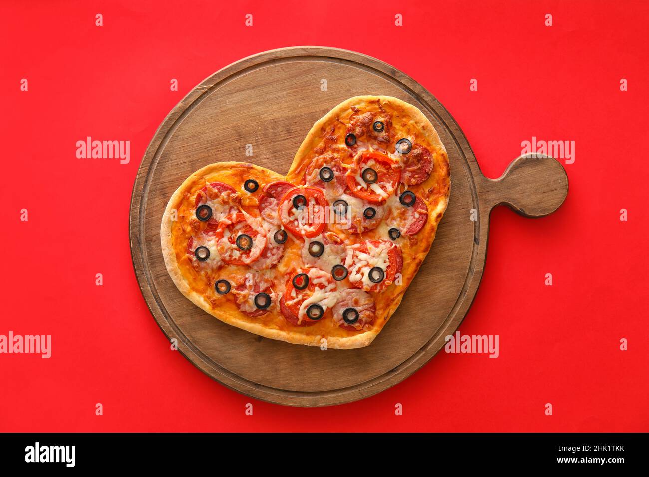 Wooden board with tasty heart-shaped pizza on red background. Valentine ...