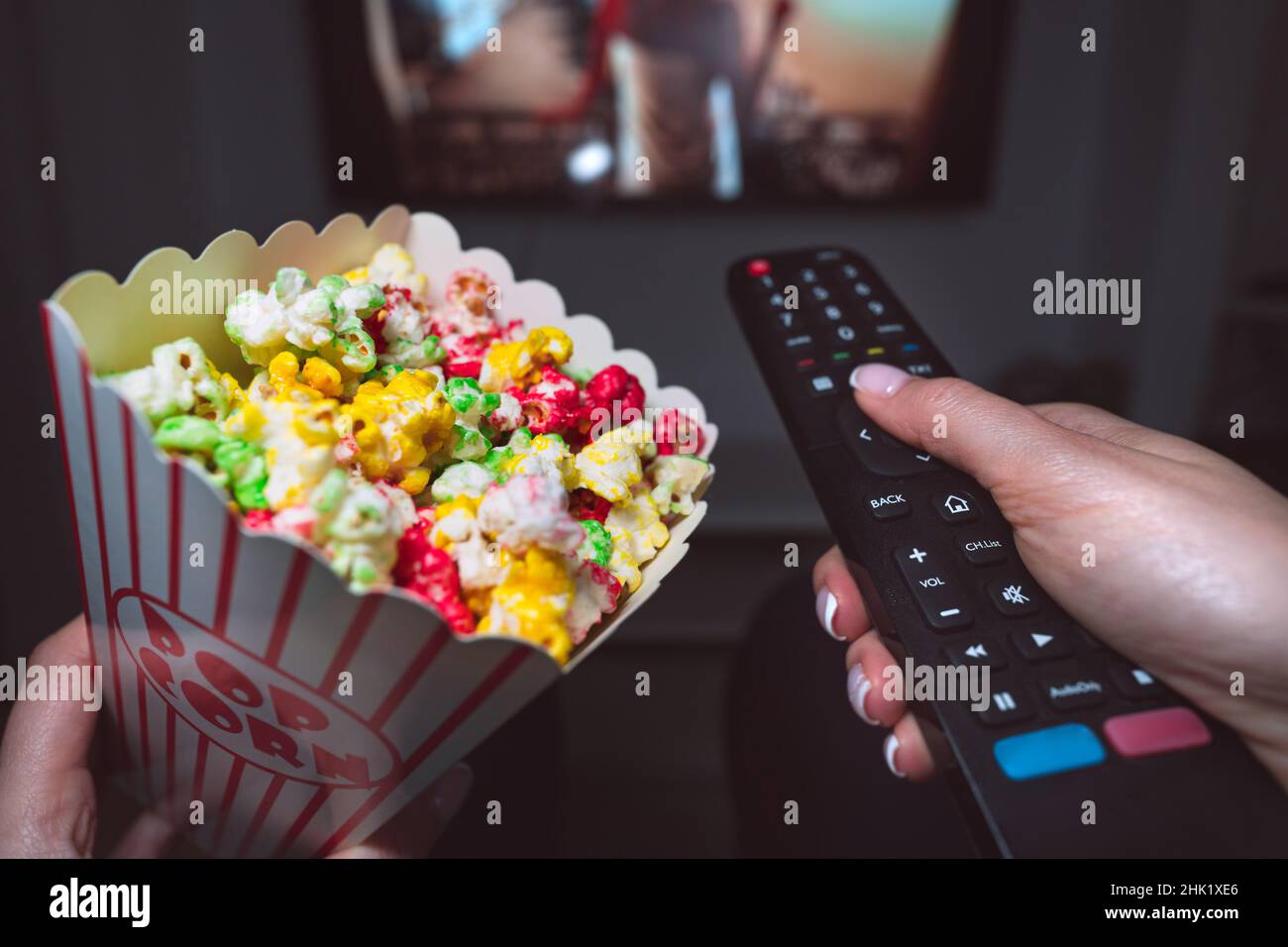 Woman watching TV or watching movie with remote control and popcorn at home. First person view ...