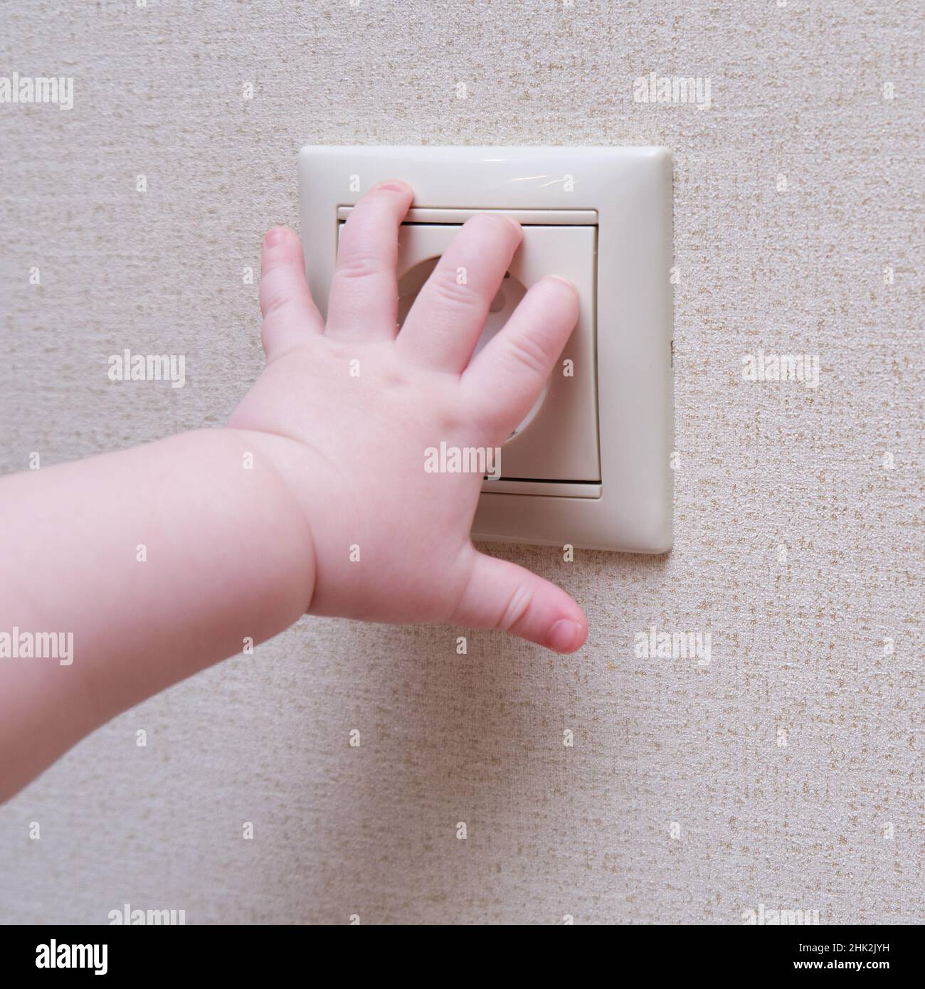 Baby toddler reaches into the electrical outlet on the home wall with ...