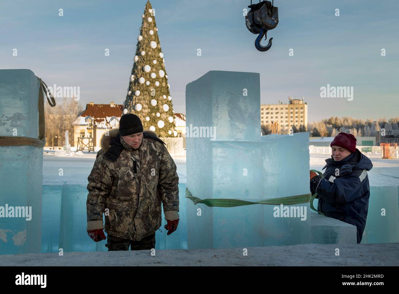 Workers in winter suits wind slings under an ice block at a ...