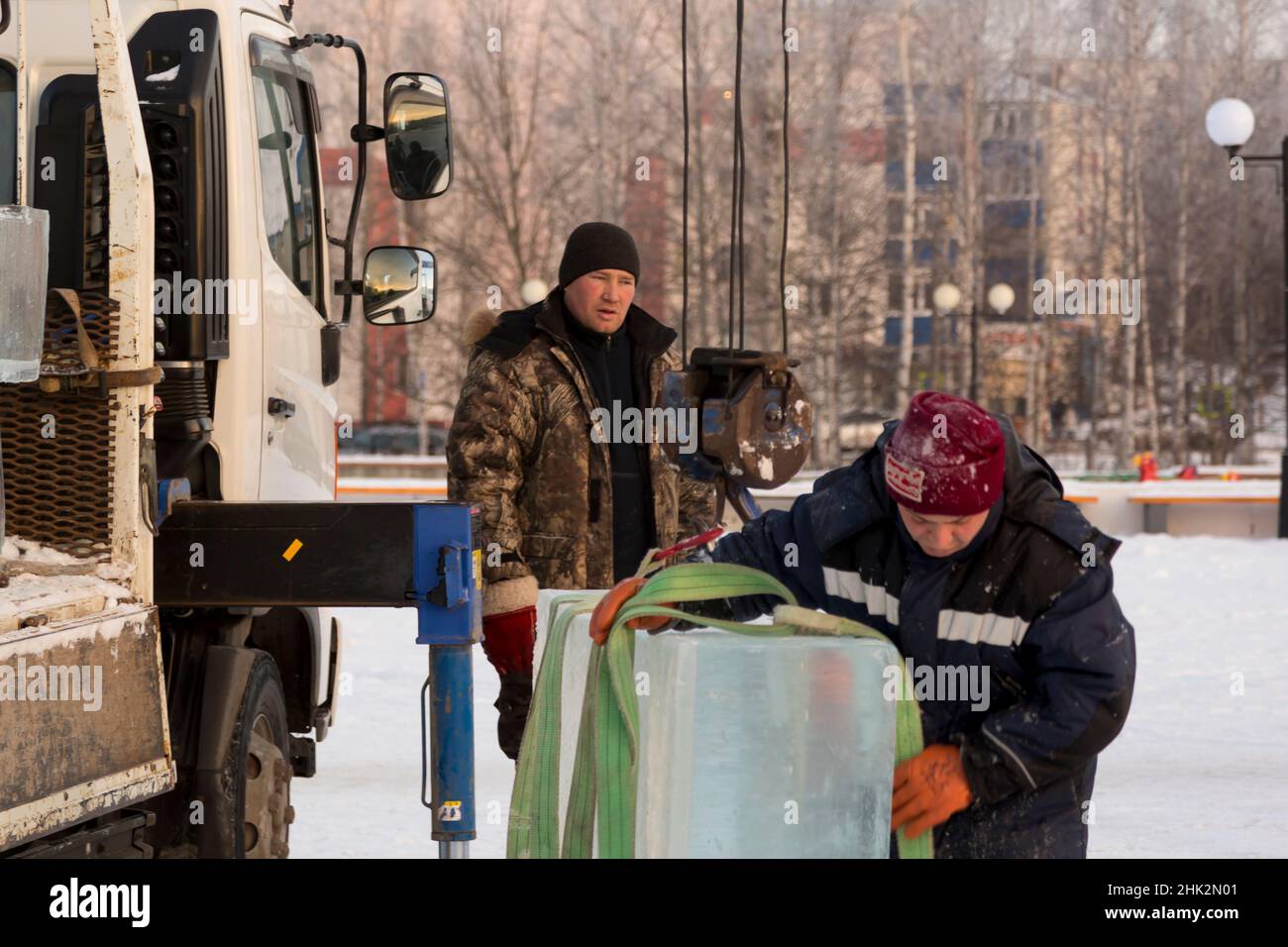 Workers in winter suits wind slings under an ice block at a ...