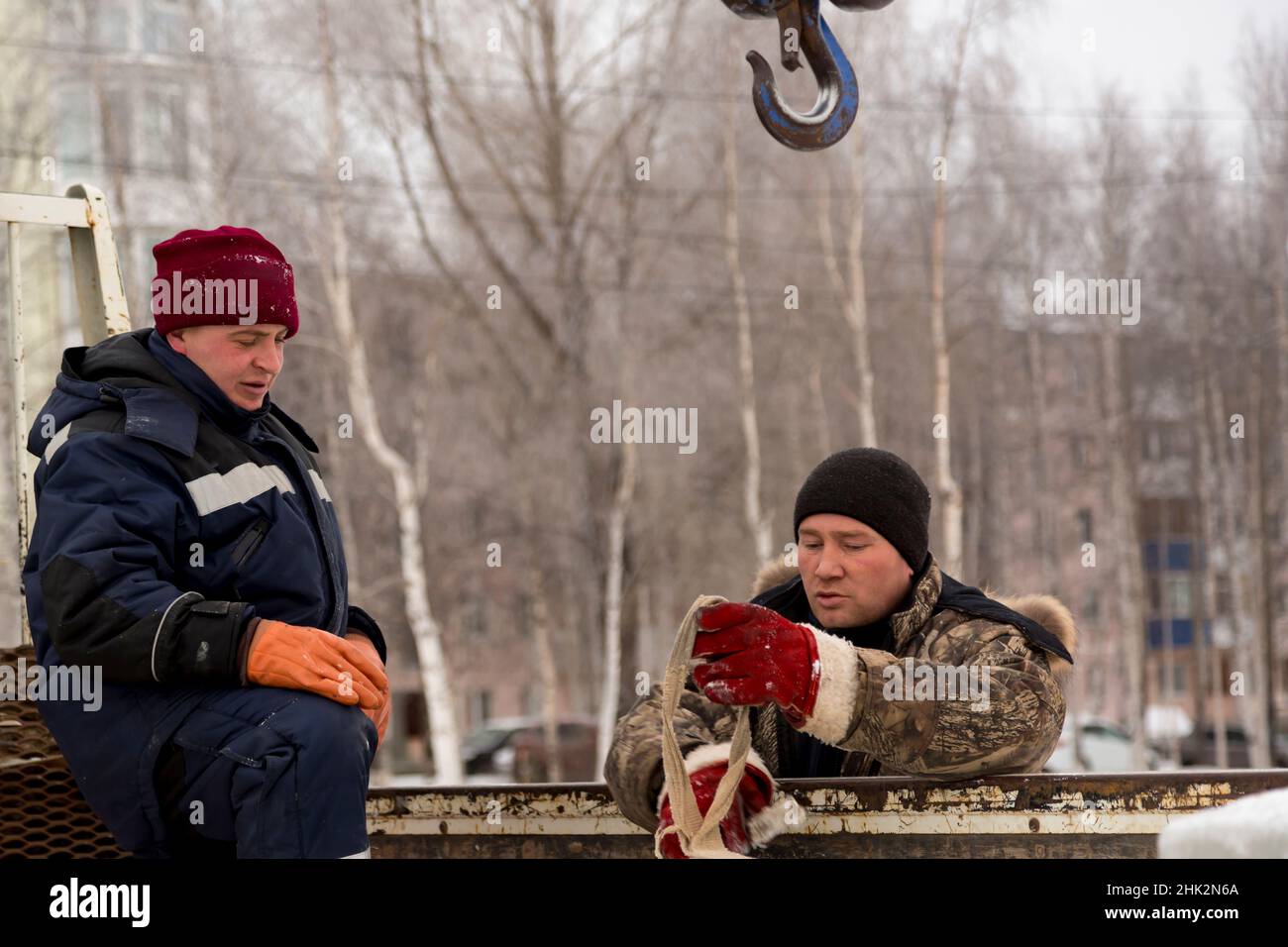 Workers in winter suits wind slings under an ice block at a ...
