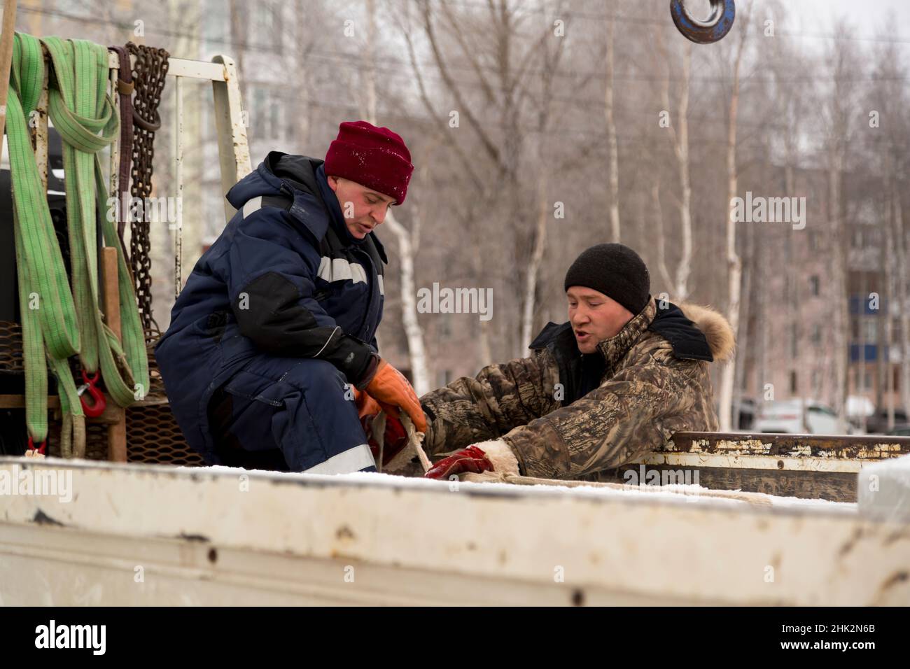 Workers in winter suits wind slings under an ice block at a ...