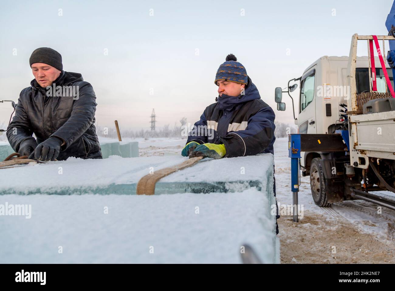 Workers in winter suits wind slings under an ice block at a ...