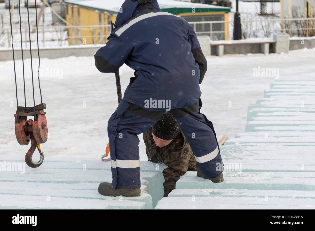 Workers in winter suits wind slings under an ice block at a ...