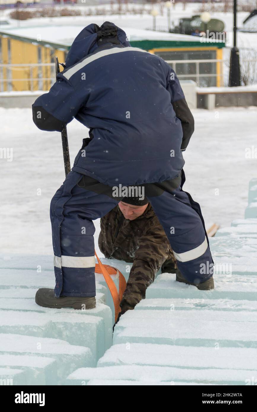 Workers in winter suits wind slings under an ice block at a ...