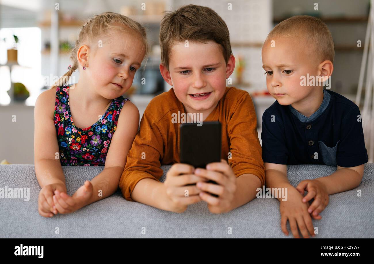 Portrait of children playing on mobile phone together at home. Internet ...