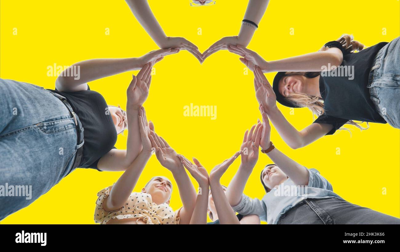 Female friends make a heart shape from their hands on a yellow ...