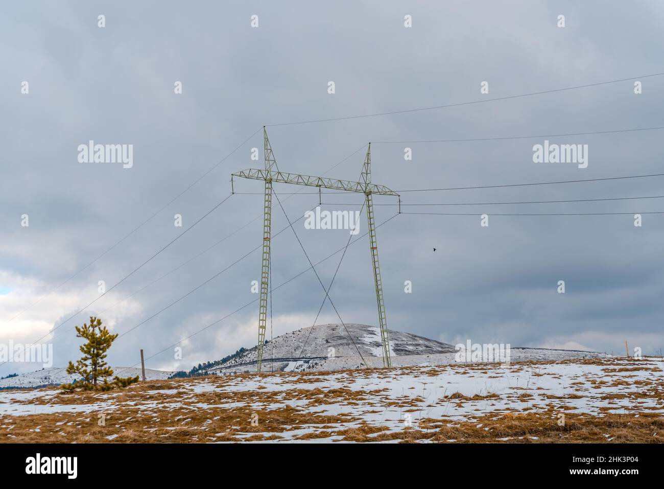 High voltage power line in the mountains with snow on mountains and dry ...