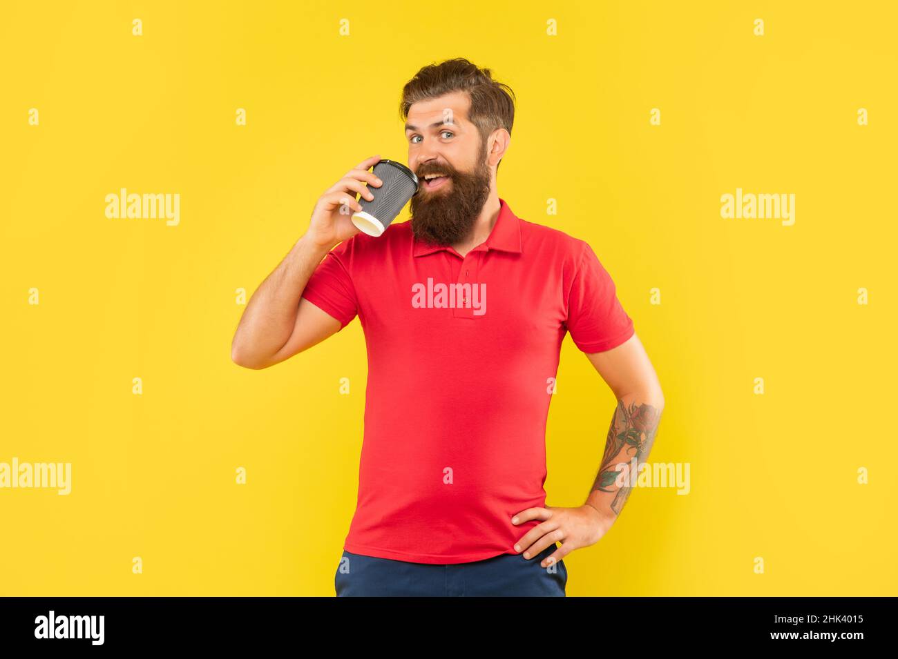 Happy man drinking coffee from disposable cup with arm akimbo yellow ...