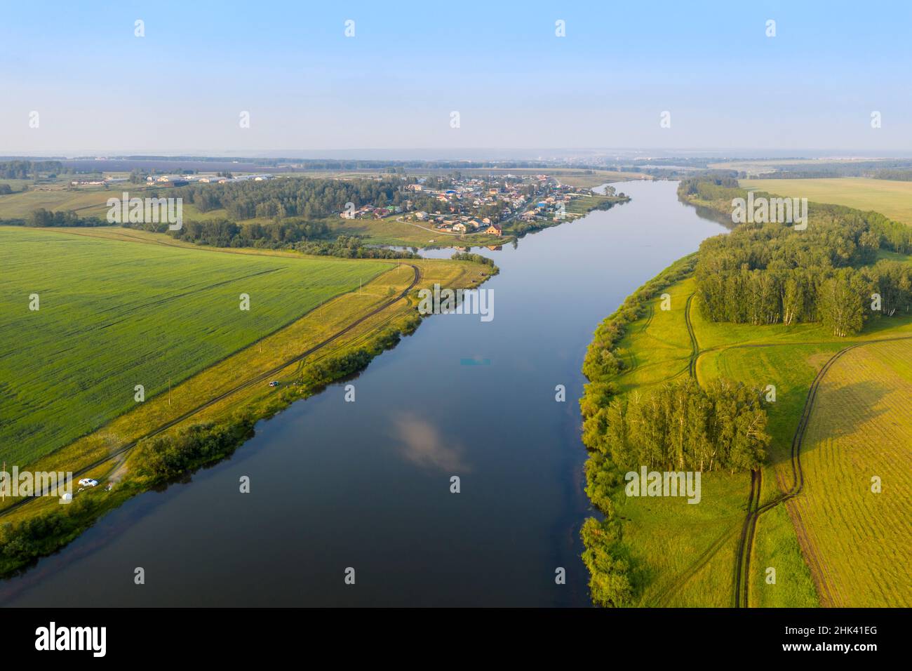 Aerial view of a wide river and a village in the distance among fields ...