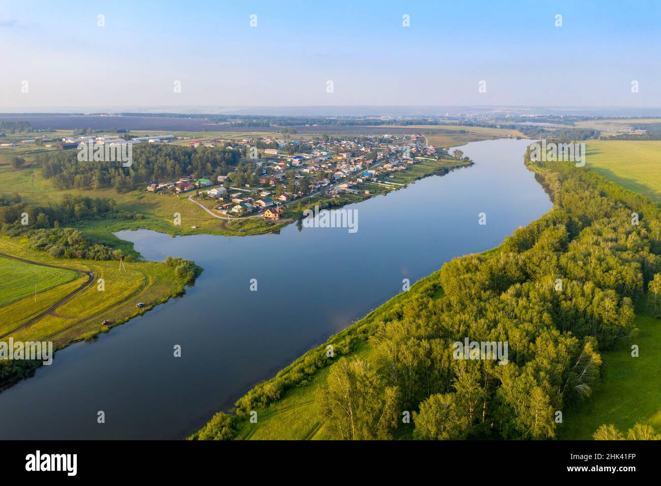 Aerial view of a wide river and a village in the distance among fields ...