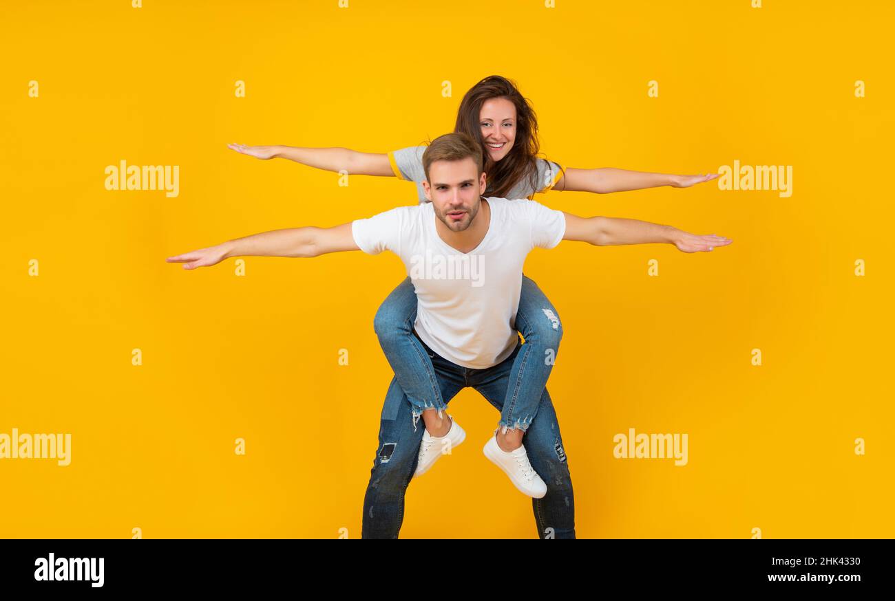Happy playful girl and guy pretend flying doing piggyback ride yellow ...