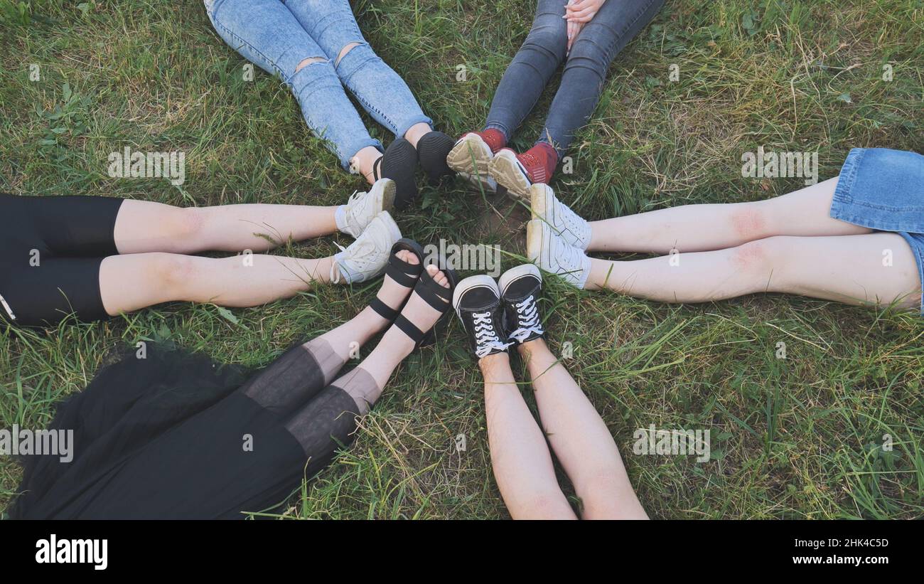 Friends are sitting on the grass with their legs joined in a circle ...