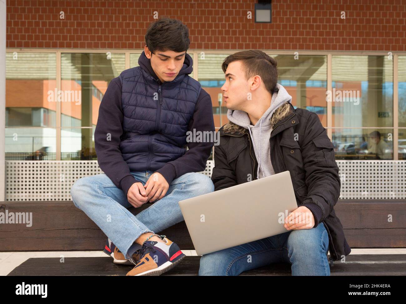 couple of student friends sitting on a bench with a laptop computer ...