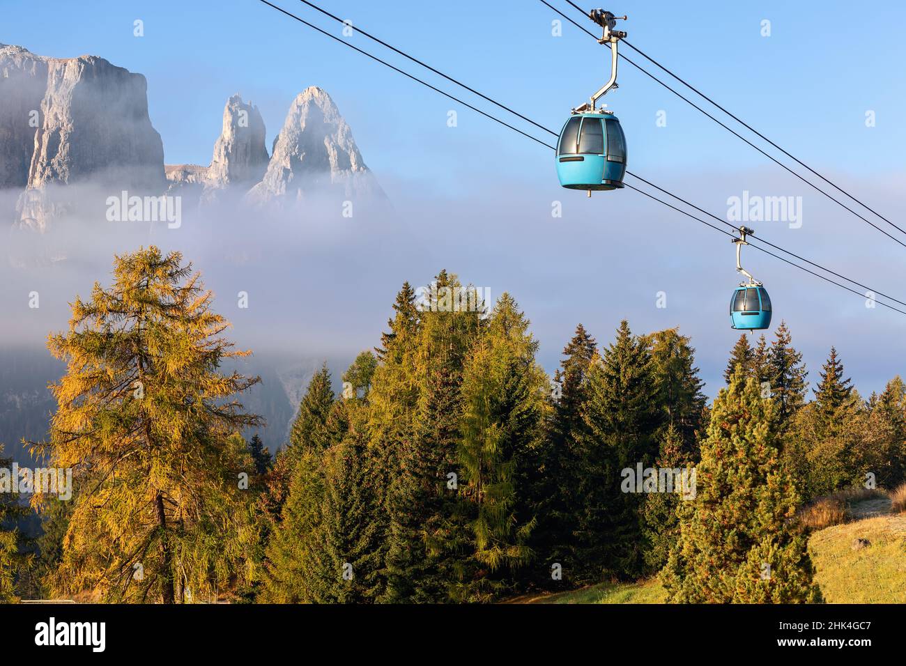 Cable car cabins over the autumn trees at the foggy morning in Seiser ...