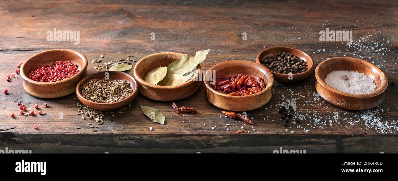 Small bowls with various spices in a row on a dark rustic wooden plank ...