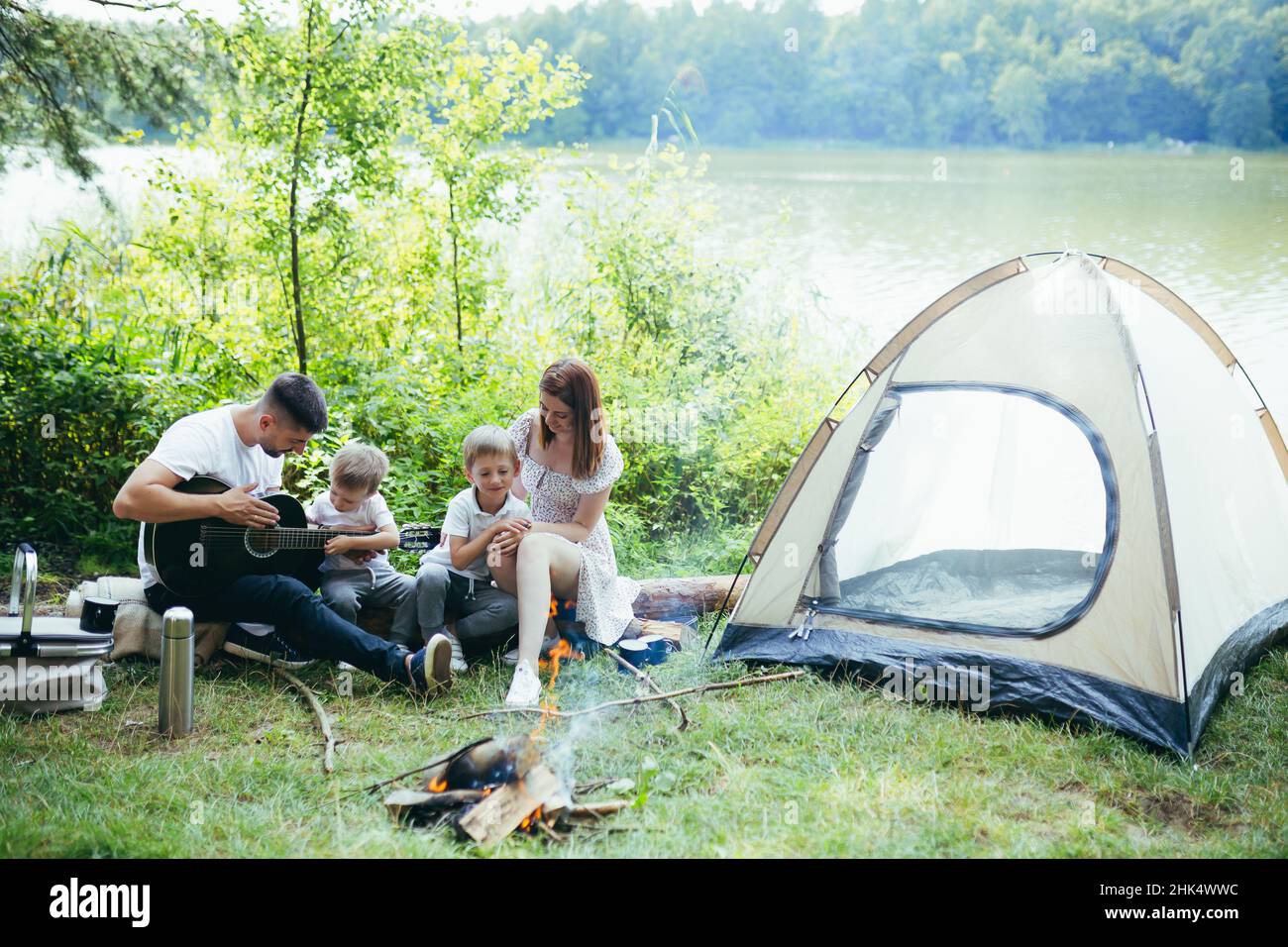 camping by lake in woods. happy family dad mom and little kids sitting ...