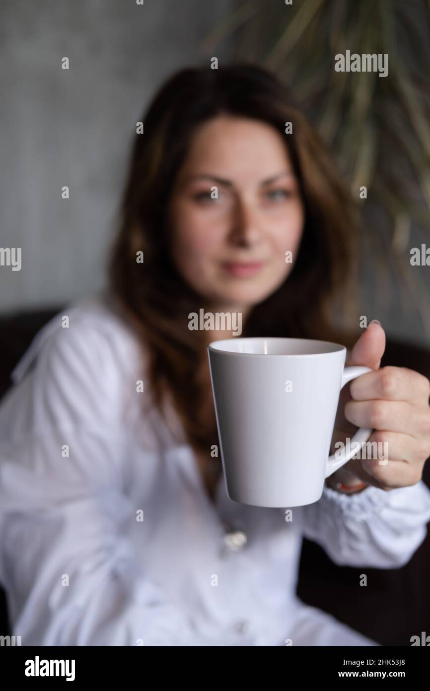 woman in white shirt on leather couch holding white cup. focus on mug ...