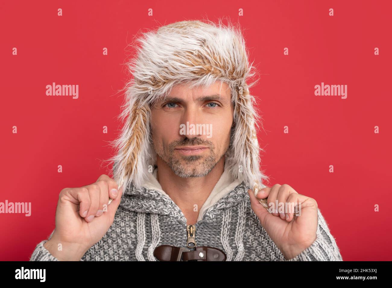 grizzled guy face in sweater and earflap hat on red background, face ...