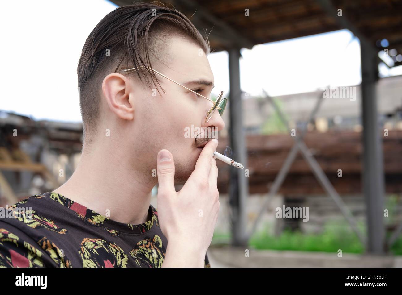 young confident man with moustache smoking a cigarette outside. bad ...