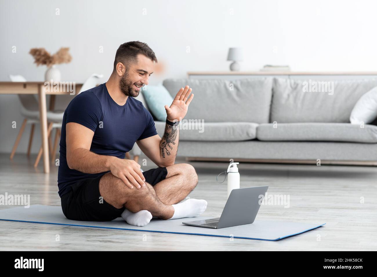 Smiling millennial muscular european man sitting on floor in lotus ...