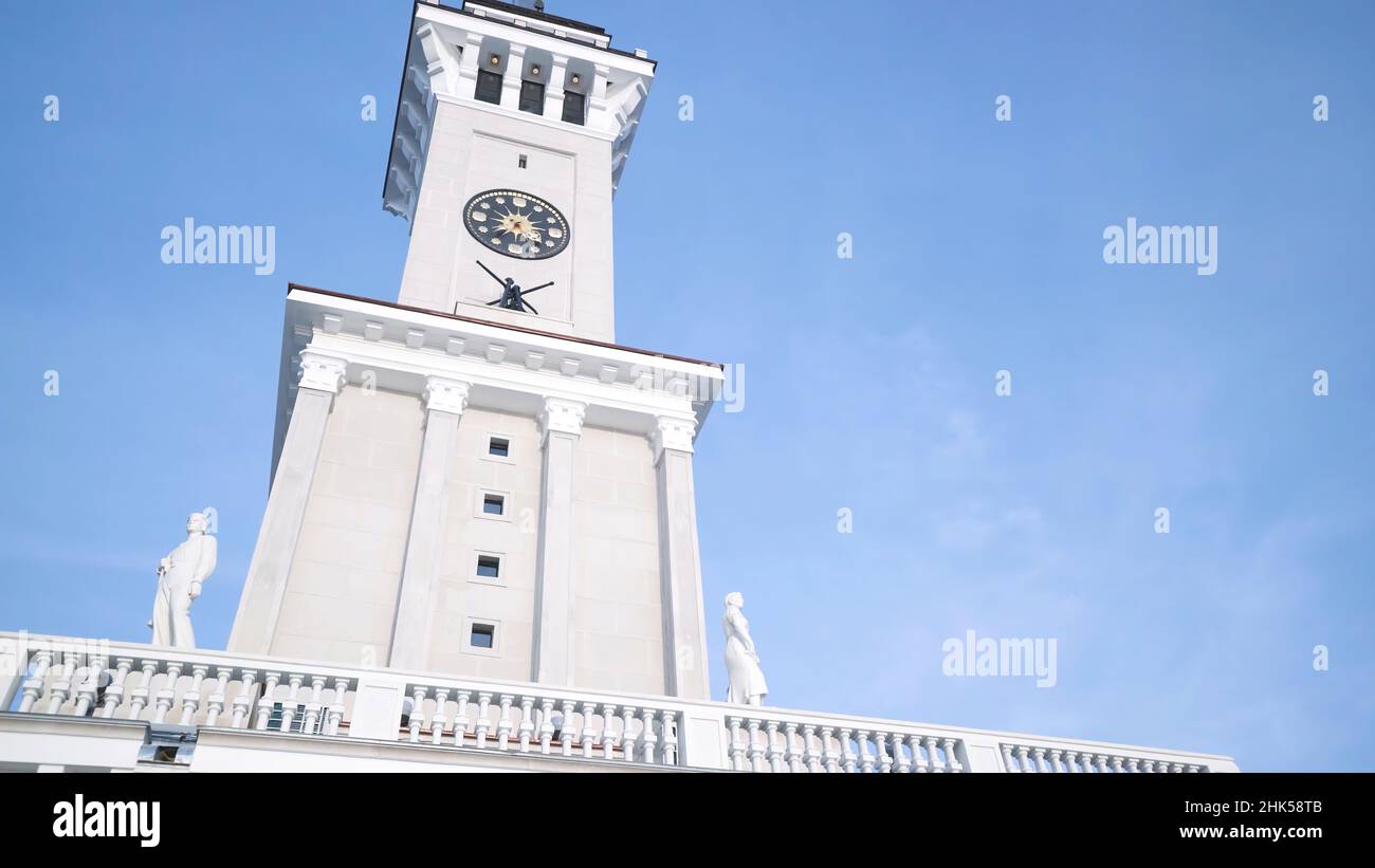 White clock tower on background of blue sky. Action. Bottom view of ...