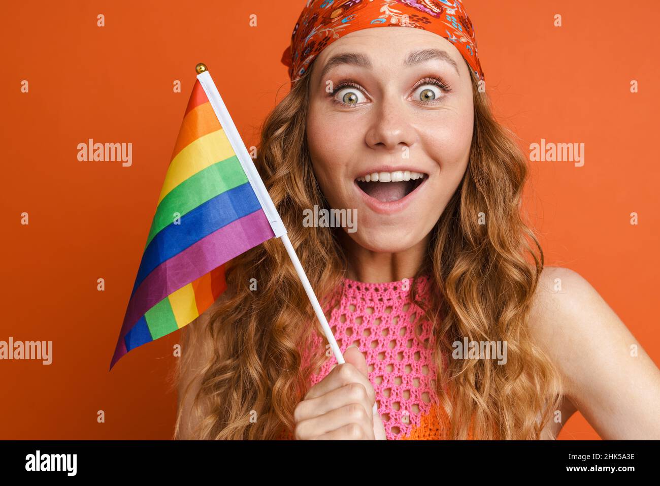 Young ginger woman expressing surprise while posing with rainbow flag ...