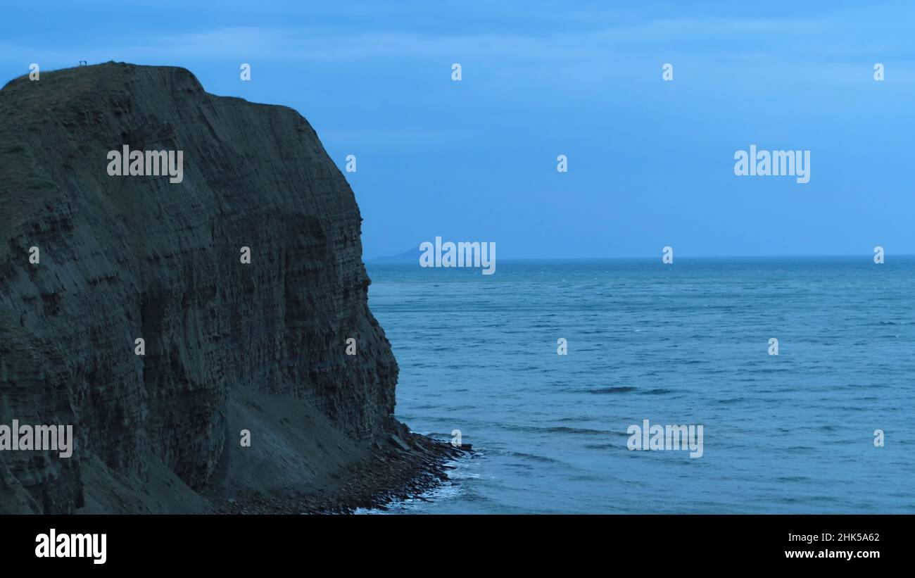Aerial view of the large grey cliff and sea waves breaking on the rocks ...