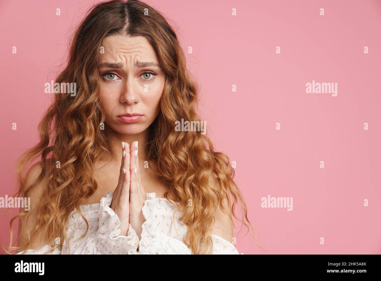 Young ginger woman wearing dress frowning while making praying gesture ...