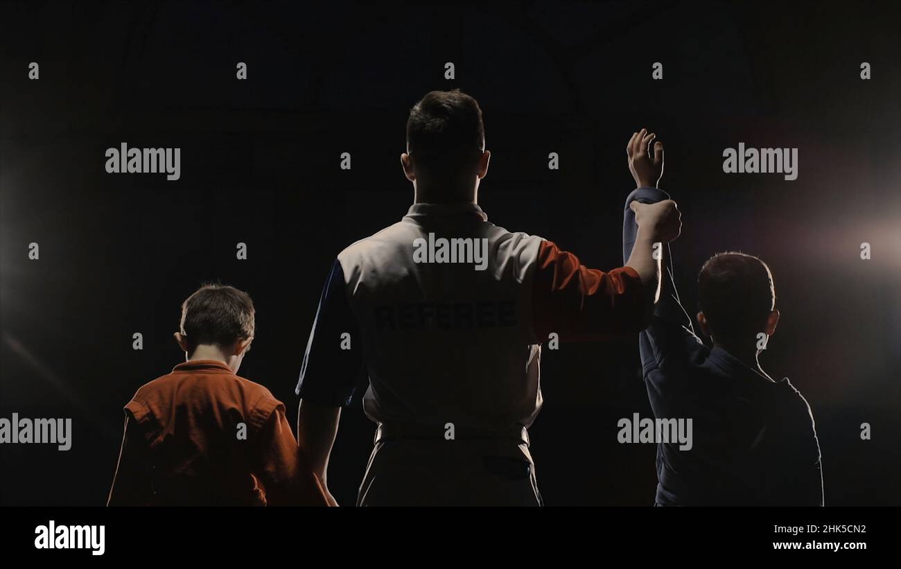 Rear view of the boys athletes and referee who raises the hand of the ...