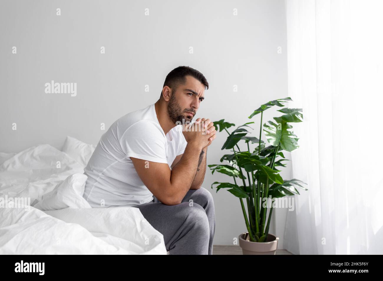 Pensive sad tired millennial muscular european male sitting on bed ...