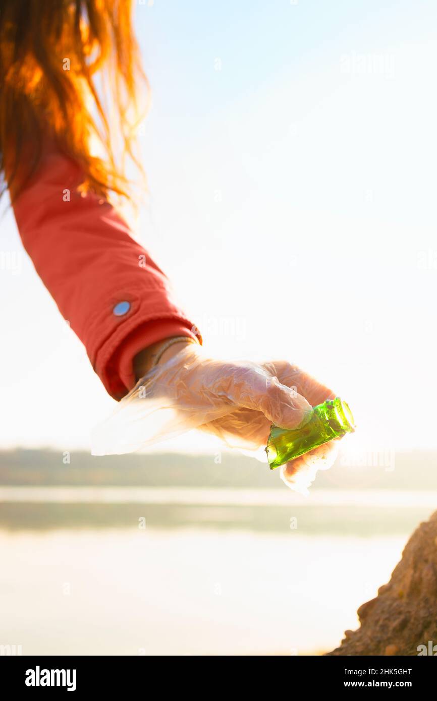 Female volunteer picking up glass waste from the beach Stock Photo - Alamy