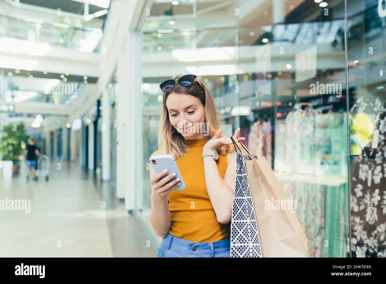 Young woman consumer in the mall browses chat and uses using a smartphone. female standing with ...