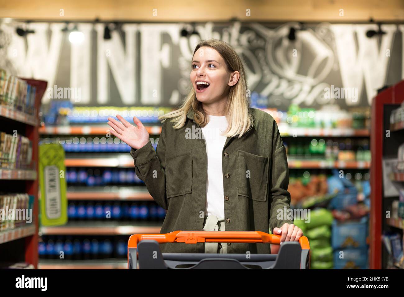 young happy woman pushing trolley spends time in a supermarket or mall ...