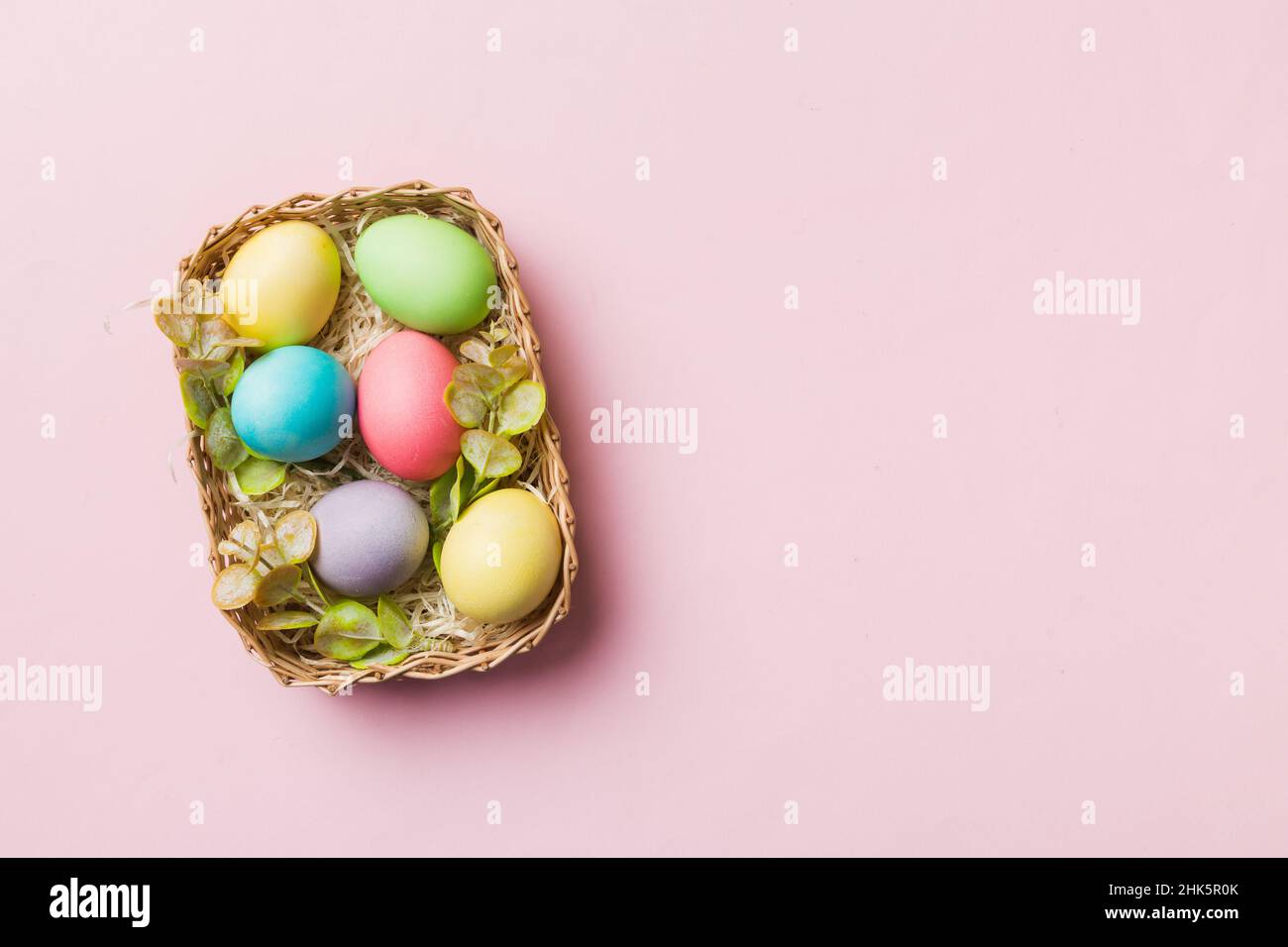 Multi colors Easter eggs in the woven basket on colored background ...