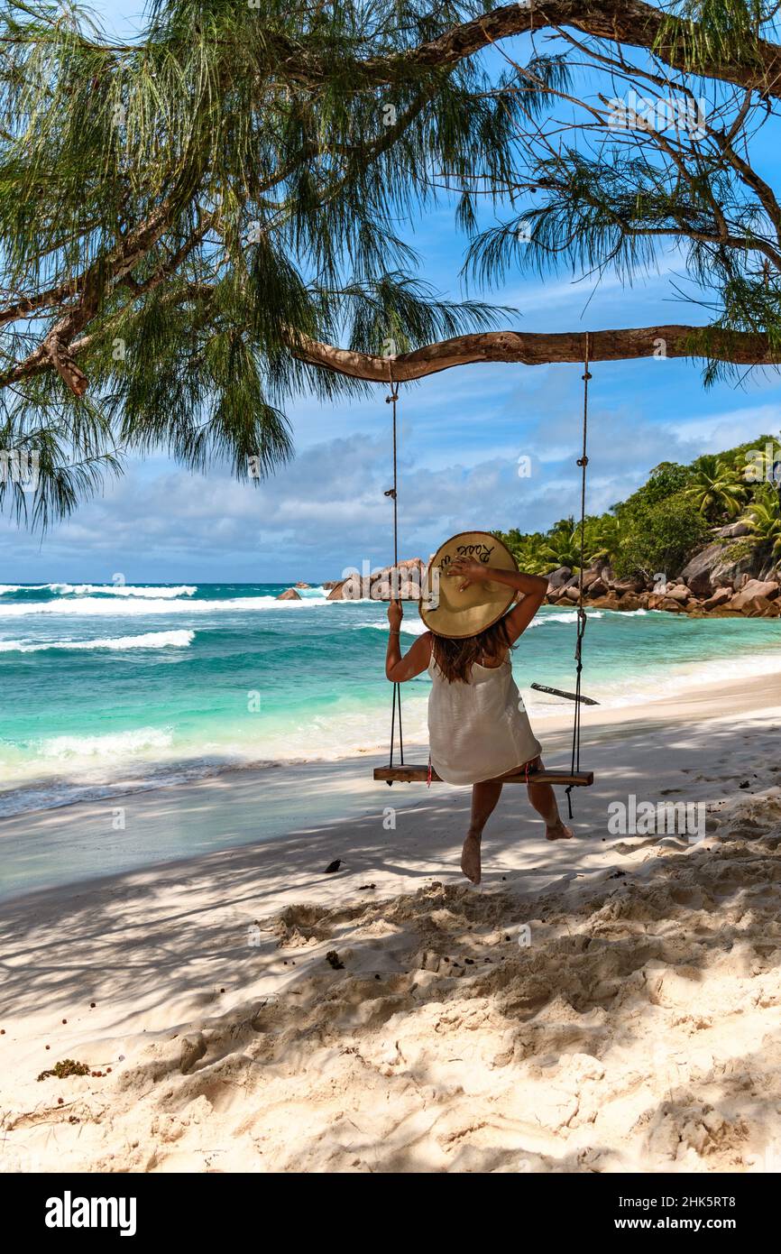 Rear view of young woman wearing beach clothes, sitting on swing on ...