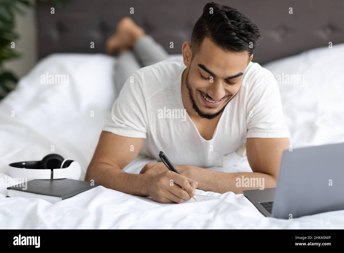 Portrait Of Arab Man Writing In Notepad And Using Laptop In Bed Stock ...