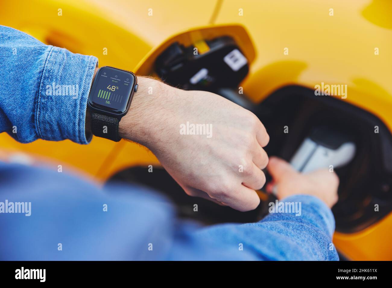 Man Charging Electric Vehicle With Cable Looking At App On Smart Watch ...