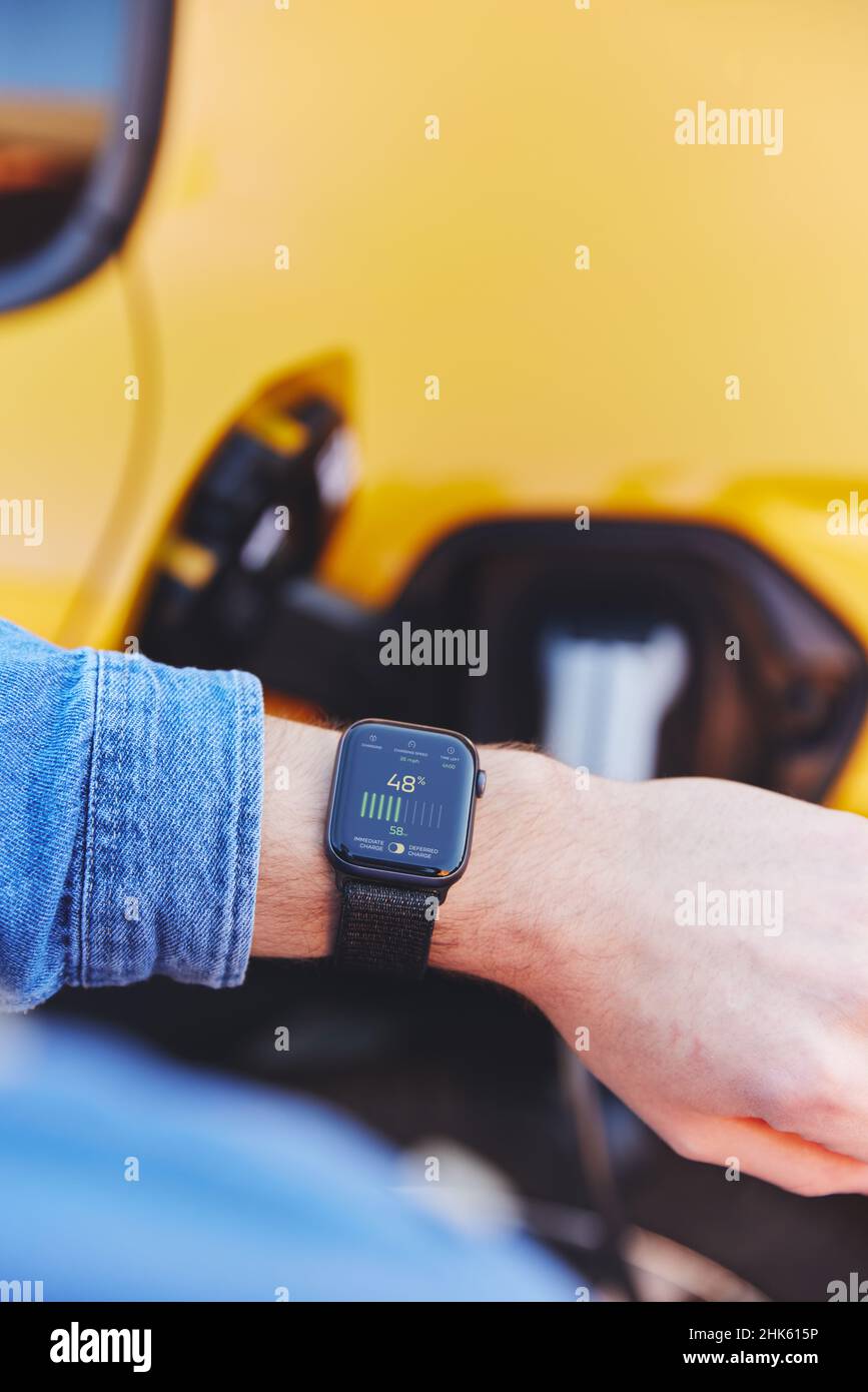 Man Charging Electric Vehicle With Cable Looking At App On Smart Watch ...